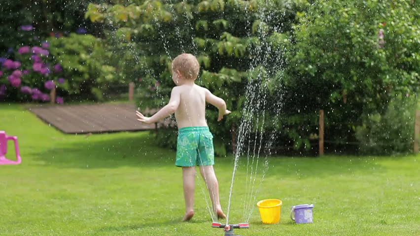 Little Boy Playing With Garden Sprinkler And Umbrella In The Backyard ...